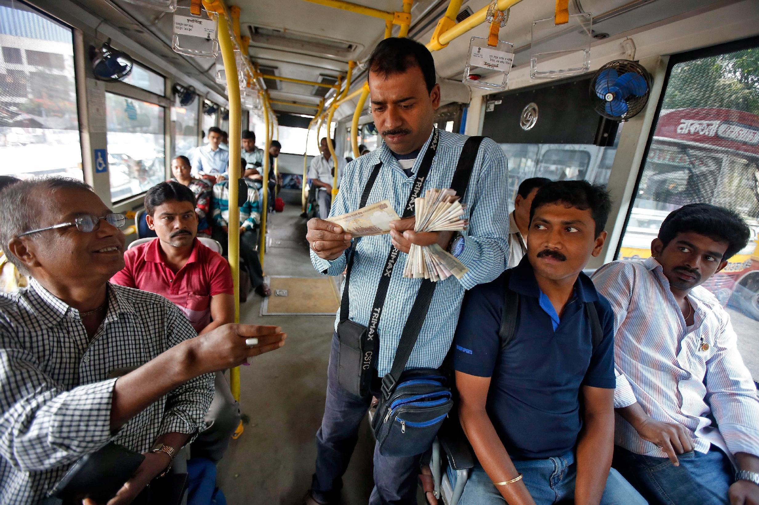 A government bus conductor checks a 500 Indian rupee banknote before ...